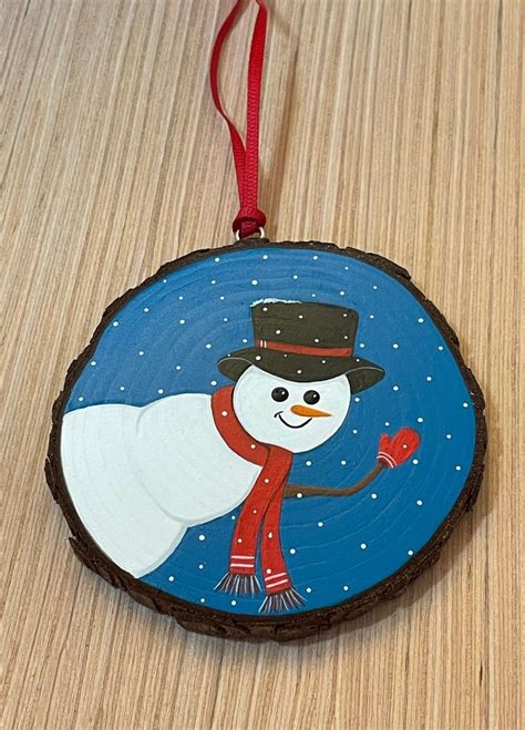 A Wooden Ornament With A Snowman Wearing A Hat And Scarf On It
