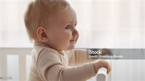 귀여운 아기의 초상화는 유아용 침대에 서서 옆으로 미소 짓고 호기심 파노라마 빈 공간을 바라보며 아기에 대한 스톡 사진 및 기타 이미지 Istock