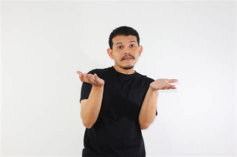 젊은 성인 아시아 남성이 팔을 들고 의심스러운 얼굴로 카메라를 바라보고 있다 스튜디오 촬영 밝은 회색 배경에 격리되어 있습니다