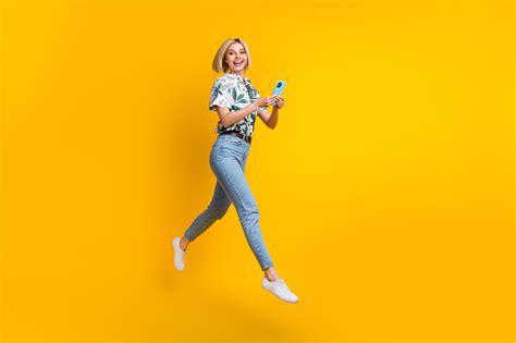 긍정적 인 예쁜 화려한 소녀 입고 인쇄 블라우스 청바지 비행 스마트 폰을 들고 노란색 배경에 고립 된 전체 크기 사진 Brand Name Smart Phone에 대한 스톡