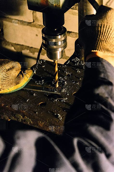 在车间工作就是在钻床上钻床的金属零件他穿着工装裤戴着脏手套