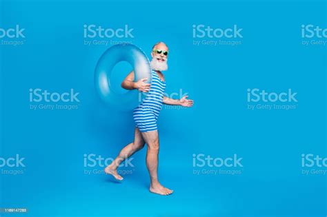 파란 배경 위에 고립 된 줄무늬 수영복을 입고 움직이는 장난감 반지를 들고 안경 안경을 들고 사랑스러운 은퇴 한 남자의 전체