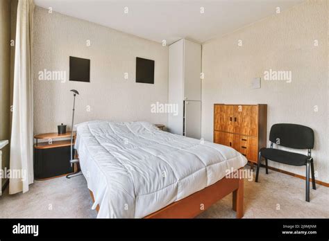 Wooden Vintage Commode Near Comfortable Bed With Blanket Placed Near Radiator In Light Bedroom