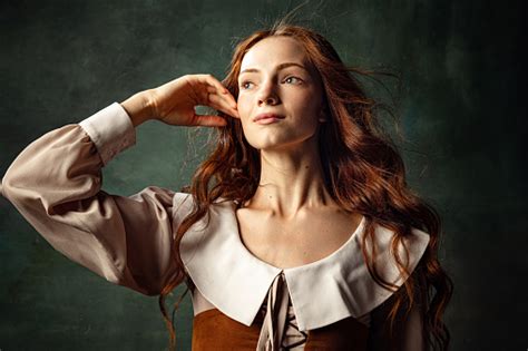 르네상스 시대의 소녀처럼 긴 곱슬 머리를 가진 매력적인 빨간 머리 소녀의 초상화 어두운 배경에 고립 된 여성 농민 시대 비교 아름다움 예술 20 24세에 대한 스톡 사진 및