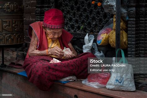 카트만두 부다나트 스투파 입구의 기도 바퀴 옆에 앉아 있는 100년 된 티베트 불교 수녀 Unesco 조직된 단체에 대한 스톡