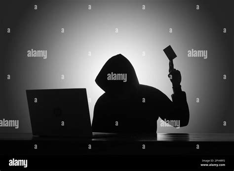 Mysterious Man Wearing Black Hoodie Using Laptop And Holding Credit Card In The Dark Room