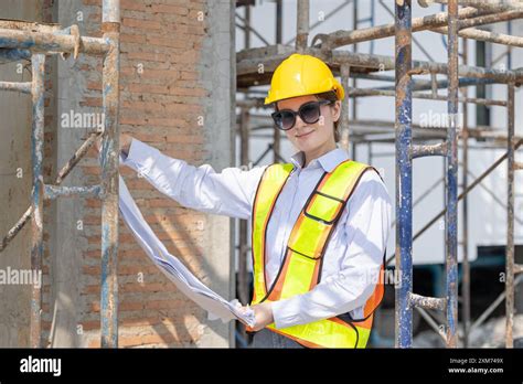 Confident Female Architect In Safety Gear Holding Blueprints And Inspecting Construction Site