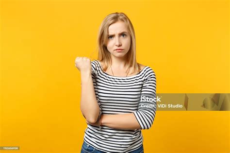 스튜디오에서 노란 주황색 벽 배경에 고립 된 주먹을 쥔 카메라를 찾고 줄무늬 옷에 관련 된 젊은 여자의 초상화 사람들은 진심으로 감정 라이프 스타일 개념입니다 복사 공간을