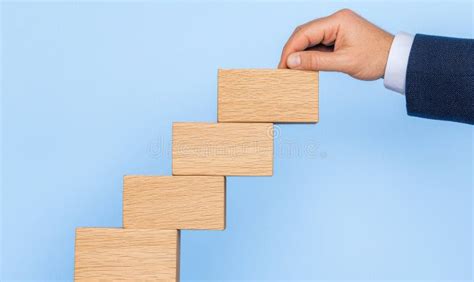 A Hand Placing A Wooden Block On A Staircase Of Blocks Representing Growth And Success Stock