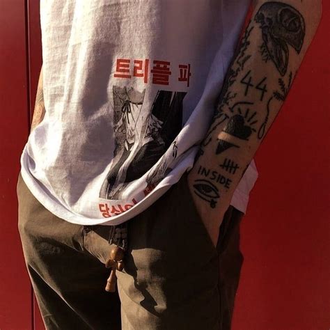 A Man With Tattoos On His Arm Standing In Front Of A Red Wall And Wearing Shorts