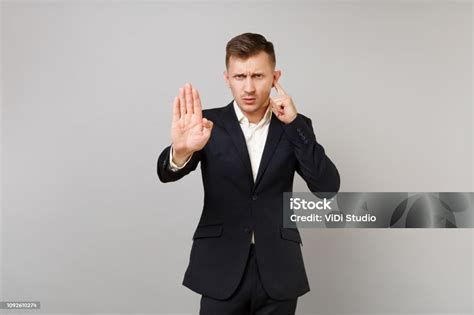 우려 젊은 비즈니스 남자가 고전적인 검은 양복 손가락으로 귀를 덮고 손바닥 회색 배경에 고립 중지 제스처를 보여주는 있다 성과