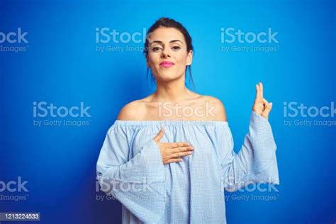 파란색 고립 된 배경 위에 롤빵 헤어 스타일을 입고 젊은 아름다운 여성은 가슴과 손가락에 손을 맹세 충성 약속 맹세를 만들기 갈색 머리에 대한 스톡 사진 및 기타 이미지