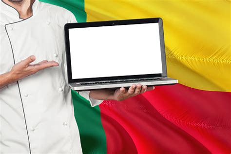 베냉 국기 배경에 빈 화면으로 노트북을 들고 Beninese 요리사 복사 공간에 대 한 유니폼과 포인팅 노트북을 입고 요리 고급 요리에 대한 스톡 사진 및 기타 이미지