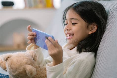 A Young Girl Is Sitting On A Couch And Playing A Video Game On Her