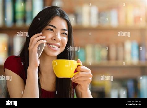 Cheerful Korean Girl Talking On Cellphone And Drinking Coffee At Cafe