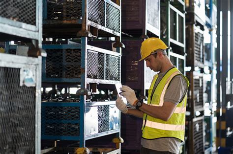 유통 창고 컴퓨터 및 남성 창고 작업자가 안전 유니폼 헬멧을 착용하고 보관 창고에서 노트북 컴퓨터로 제품의 품질을 검사하는 체크리스트 공장 산업 건물에 대한 스톡 사진 및