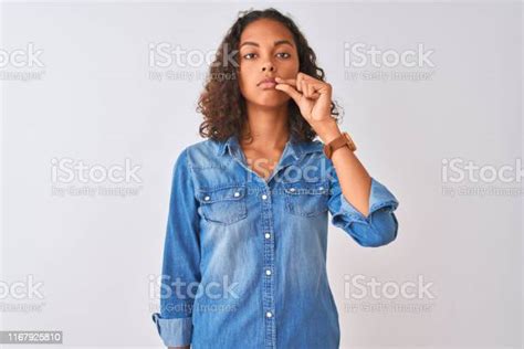고립 된 흰색 배경 입과 입술 위에 서있는 데님 셔츠를 입은 젊은 브라질 여성은 손가락으로 지퍼로 닫습니다 비밀과 침묵 금기