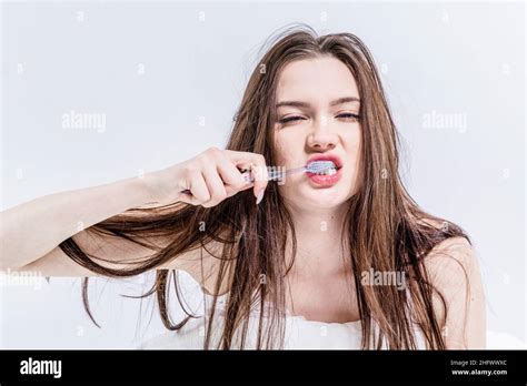 Sleepy Brunette Woman Brushes Her Teeth While Sitting On The Bed In The White Bedroom The Girl