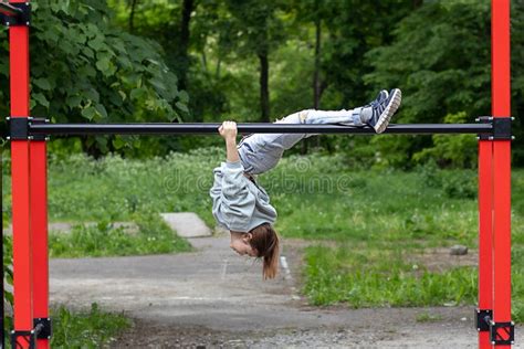 A Fitness Girl Hangs Upside Down On A Horizontal Bar In A Street Gym