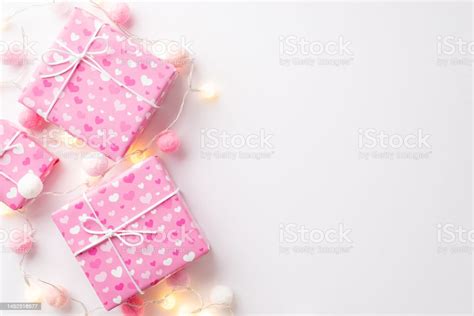 발렌타인 데이 개념입니다 하트 패턴 전구 화환과 빈 공간이 있는 격리된 흰색 배경에 푹신한 퐁퐁이 있는 포장지에 분홍색 선물 상자의 상위 뷰 사진 0명에 대한 스톡 사진 및