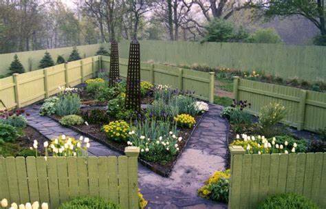 A Garden With Many Different Types Of Flowers And Trees In Its Fenced Area