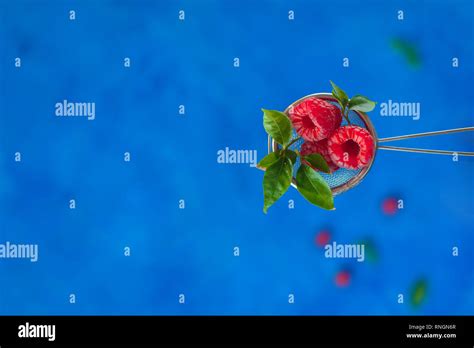 Fresh Raspberry Berries In A Steel Strainer On Vibrant Blue Background