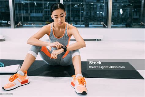 매력적인 아시아 Sportswoman 매트에 앉아서 보고 체육관에서 피트 니스 추적기 건강한 생활방식에 대한 스톡 사진 및 기타