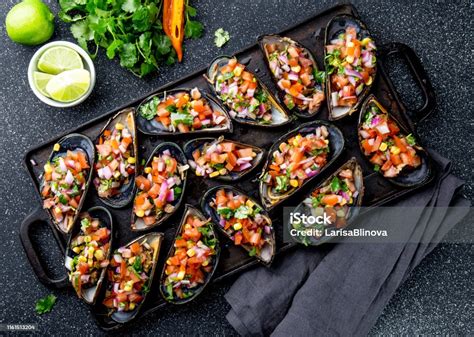 페루 음식 초로스 라 샬라카 큰 홍합 보라색 양파 토마토 옥수수 레몬으로 조미한 초로스 자파토 맨 위 보기 검은 색 배경입니다 전통 페루 요리 가리비에 대한 스톡 사진 및