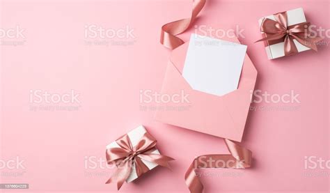 발렌타인 데이 장식의 상단 보기 사진은 분홍색 활 곱슬 실크 리본과 빈 공간이있는 고립 된 파스텔 핑크 배경에 종이 시트가있는 열린 분홍색 봉투가있는 흰색 선물 상자 두