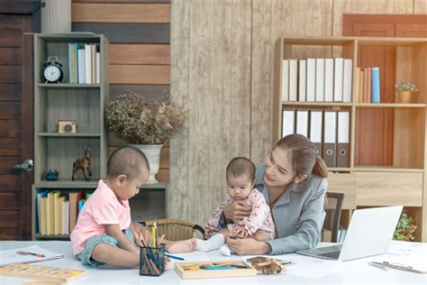 바쁜 여자는 두 아이를 돌보는 동안 일을하려고 젊은 아시아 어머니는 이야기하고 그녀의 주위에 놀고 두 아이와 함께 재생 멀티