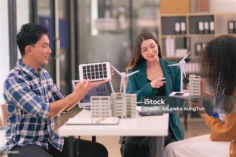 풍력 터빈과 함께 만나는 엔지니어 팀은 풍력 터빈과 함께 태양 전지판이 있는 테이블 위에 놓인 주택 모델과 청사진을 사용하여