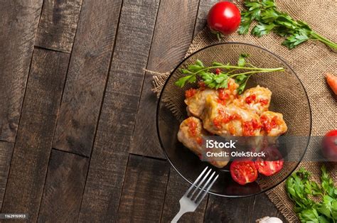 삶은 양배추 롤의 한 부분은 검은 유리 판에 쌀과 고기로 채워진 것 중 하나이며 금속 포크는 채소 근처의 채소와 소박한 나무 테이블위에 있습니다 갈색에 대한 스톡 사진 및