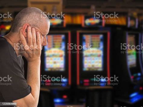슬프고 우울한 백인 남자는 카지노 슬롯 머신의 행 앞에서 그의 머리에 자신의 손으로 앉아 도박 중독 테마 이미지 슬롯머신에 대한 스톡 사진 및 기타 이미지 Istock
