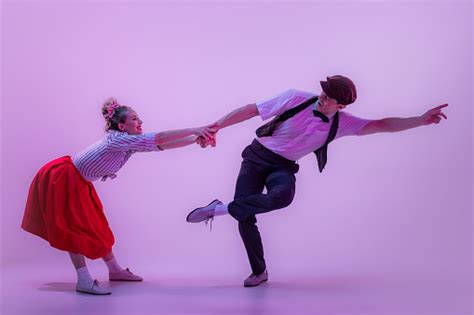 빈티지 복고풍 스타일의 의상을 입은 젊은 남녀의 스튜디오 샷은 네온 라이트의 라일락 색상 배경에 고립 된 린디 홉을 춤추고