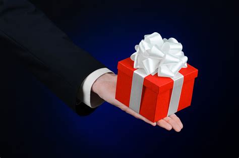 축 하와 선물의 테마 고립 된 스튜디오에 진한 파란색 배경에 흰색 리본 아름 다운 붉은 상자에 싸여 독점 선물 비싼 선물 개최 검은 양복에 남자 기념일에 대한 스톡 사진 및