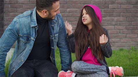 Dad And Daughter Are Sitting And Talking Against The Backdrop Of Grass And A Brick Wall Concept