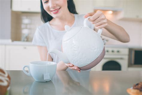테이블에 앉아 갈색 머리의 절단 보기 그녀는 흰색 주전자를 들고 컵에 물을 붓는 다 차를 준비 하 고 있는 소녀 그녀는 부엌에서