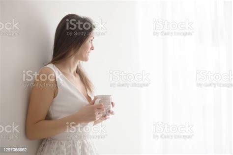 하얀 드레스를 입은 중년 여성 집에서 커피를 마시고 창 밖으로 바라보는 것 가정 생활에 대한 스톡 사진 및 기타 이미지 가정