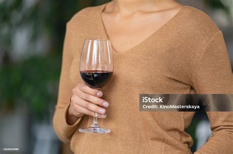 그녀의 손에 레드 와인 한 잔을 가진 인식 할 수없는 여자의 초상화 녹색 식물과 빛의 방의 흐릿한 배경에 포즈 혼합 인종 여성