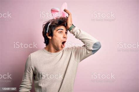 고립 된 분홍색 배경 위에 서있는 부활절 토끼 귀를 들고있는 젊은 잘 생긴 남자는 실수로 머리에 손을 대고 놀랐습니다 잊어 버린