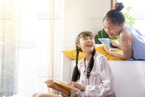 두 아름 다운 아시아 여자 자매 지출 시간을 함께 집에서 인터넷에서 디지털 태블릿을 사용하여 미소 짓는 여자와 바닥에 책을 읽고 여동생 가족 라이프 스타일과 기술 개념 2