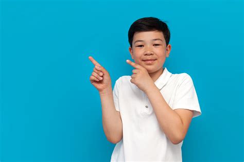 하얀 티셔츠를 입은 어린 아시아 소년이 파란 배경에 손을 옆으로 보여주고 한국 아이는 복사 공간을 광고한다 10 11세에 대한