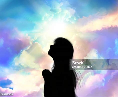 그녀의 손을 접고 하나님 께기도하는 소녀의 프로필 실루엣과 하늘에서 빛나는 신성한 빛이 있는 배경 그림 기도하기에 대한 스톡