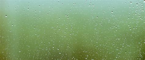 ガラスに雨滴を持つ大気の最小背景雨滴と汚れの接写で濡れた窓ぼかしたミニマリストの背景に緑のボケと汚れた窓ガラスと雨滴 しずくのストック