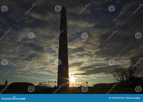 Sun Moving Behind Washington Monument Surrounded By Us Flags Against