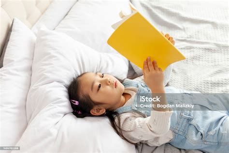 침대에 누워 노란 책을 읽는 어린 아시아 소녀 미취학 아동 한국 소녀 배우고 지식을 얻는다 중국 민족에 대한 스톡 사진 및 기타