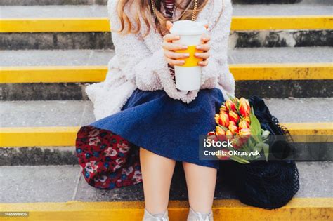 그물 가방에 재사용 가능한 커피 컵과 신선한 튤립을 들고 있는 여성의 손을 닫습니다 도시 거리의 계단에 앉아 있는 패션 여성 도시 거리 패션 봄의 분위기 선택적 초점 복사