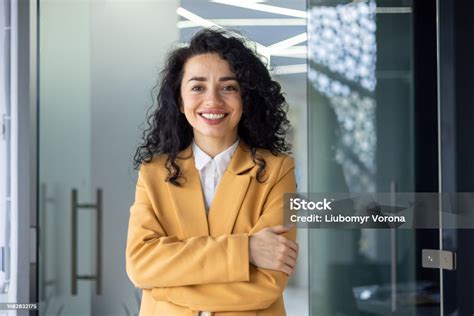 사무실 안에서 성공한 여성 사업가의 초상화 노란 양복을 입고 웃으며 카메라를 바라보는 라틴 아메리카 상사 팔짱을 끼고 서 있는