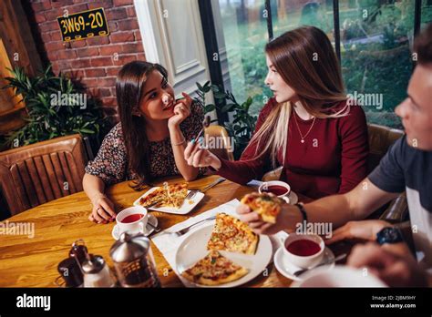 Girlfriends Are Engaged In A Conversation Eating Pizza In Cafe Stock