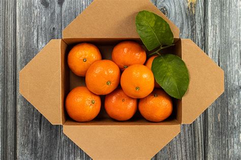 오래된 나무 테이블에 녹색 잎이있는 신선하고 유기농 귤로 가득 찬 재활용 골판지 상자의 Zenithal 샷 0명에 대한 스톡